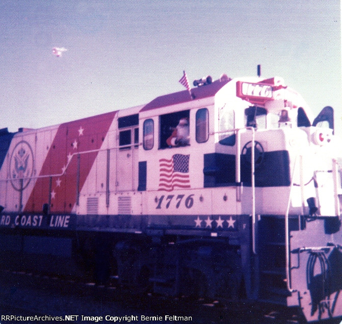 A goodie bag (to the upper left of Santa Claus) is flying from the cab of SCL U36B #1776. Santa ...